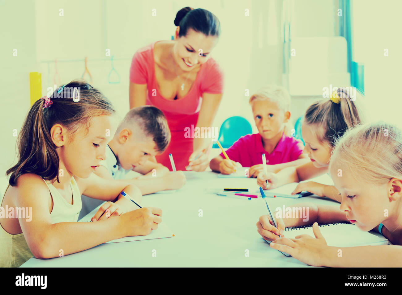 Smiling positive kids writing together with tutor at school class ...