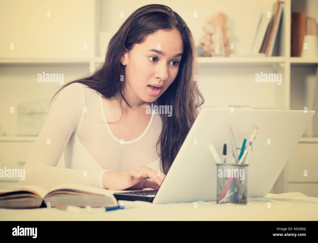 Young girl reading info in laptop and surprised indoors Stock Photo - Alamy