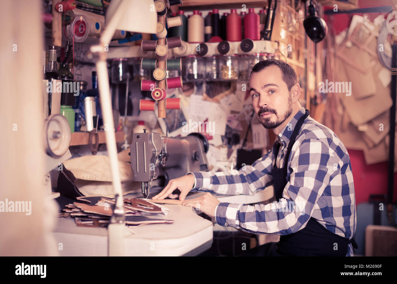 positive male worker sewing stitches on belt in leather workshop Stock ...