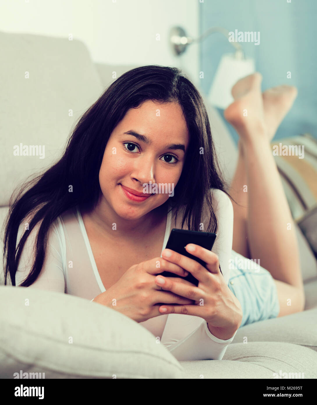 Cheerful teenager girl relaxation with phone on comfortable sofa Stock ...
