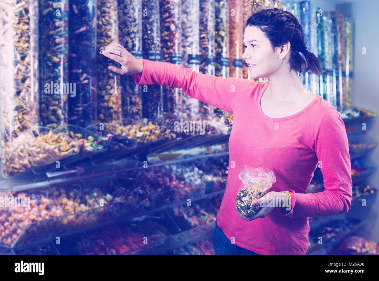 Portrait of young positive girl choosing candies for gift in sweets ...