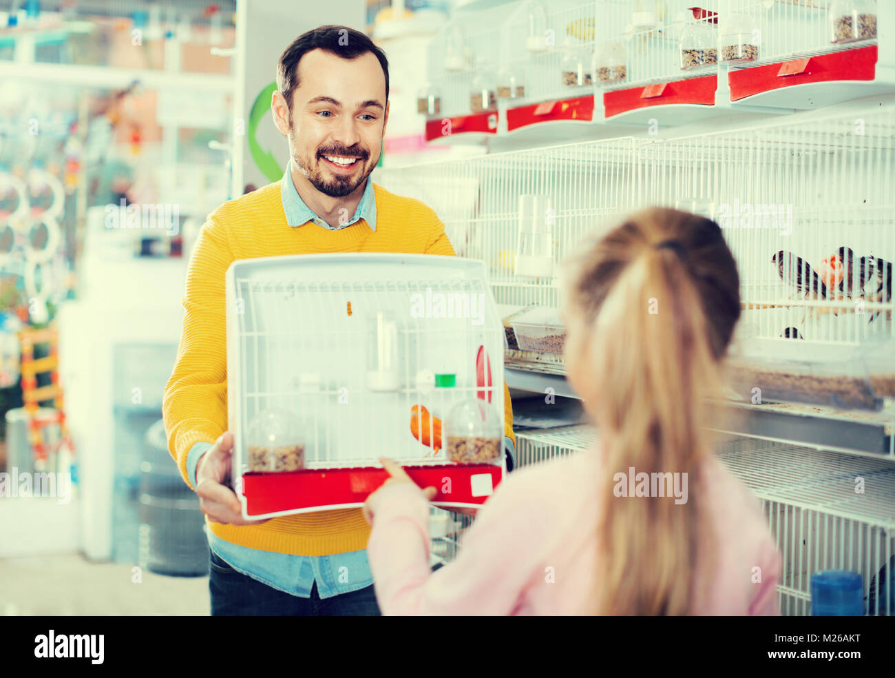 Young smiling friendly male seller showing cage with canary bird to ...
