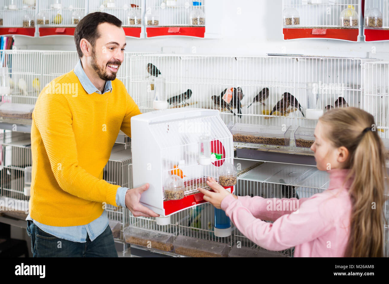 Smiling man seller demonstrating canary bird in cage to girl in pet ...