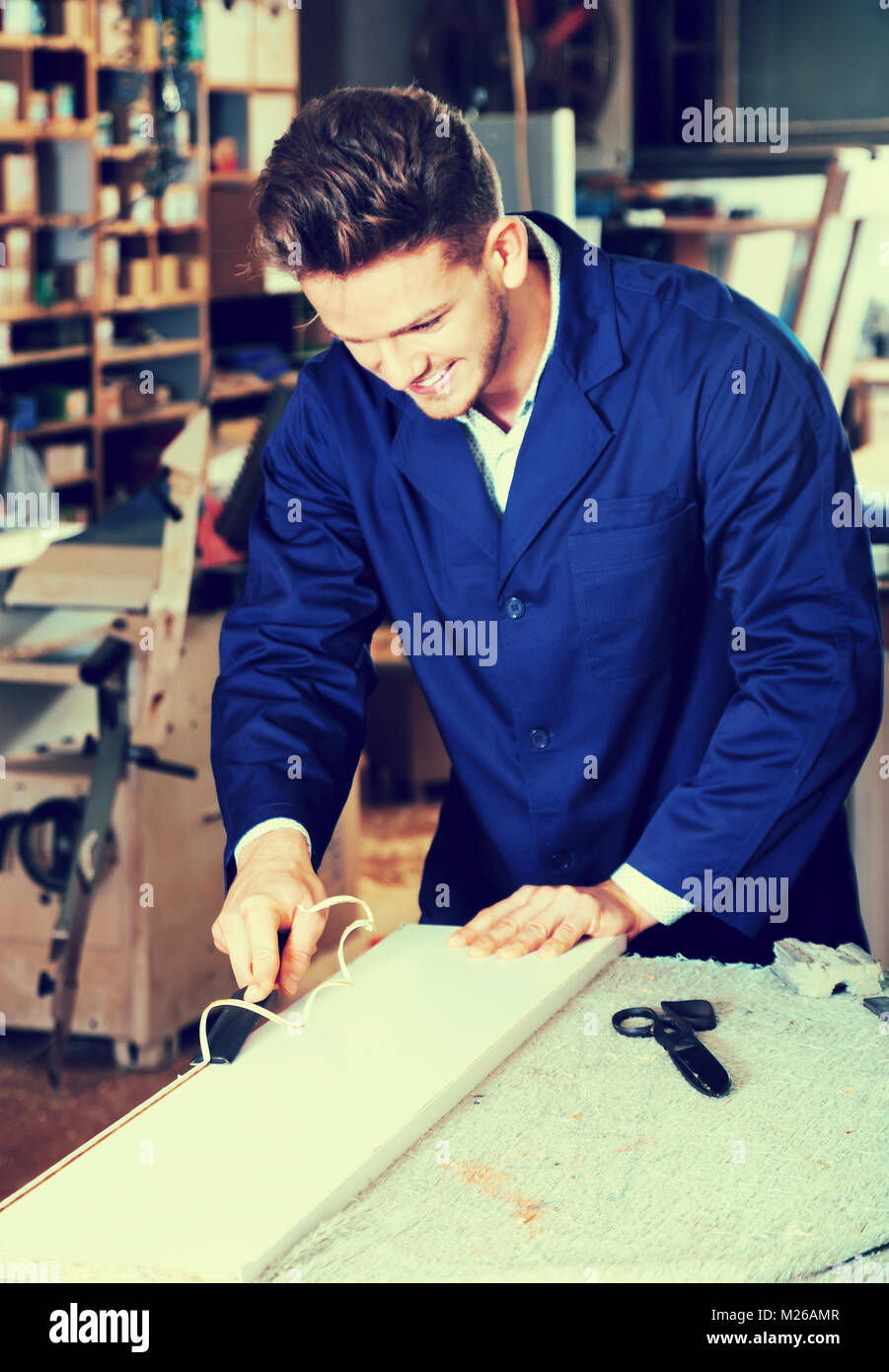Smiling male woodworker practising his skills in plank processing at ...