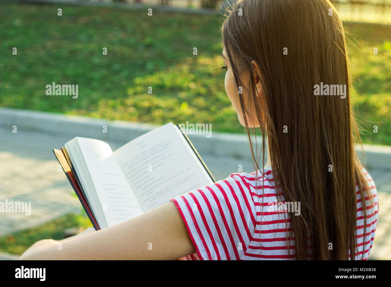 Back view of lovely young girl with long beautiful hair reading a book ...