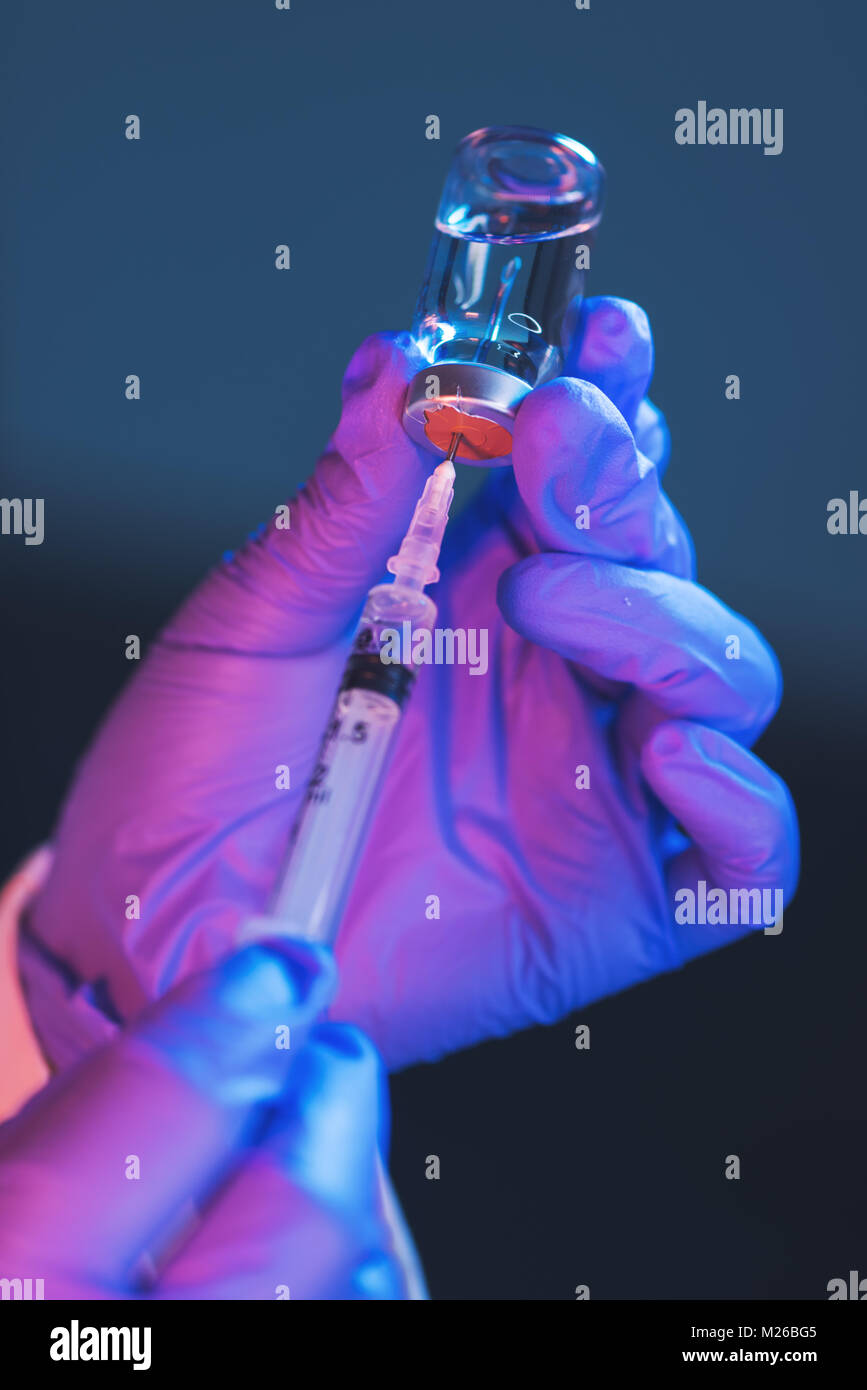 Doctor drawing up solution from vaccine bottle and filling syringe ...