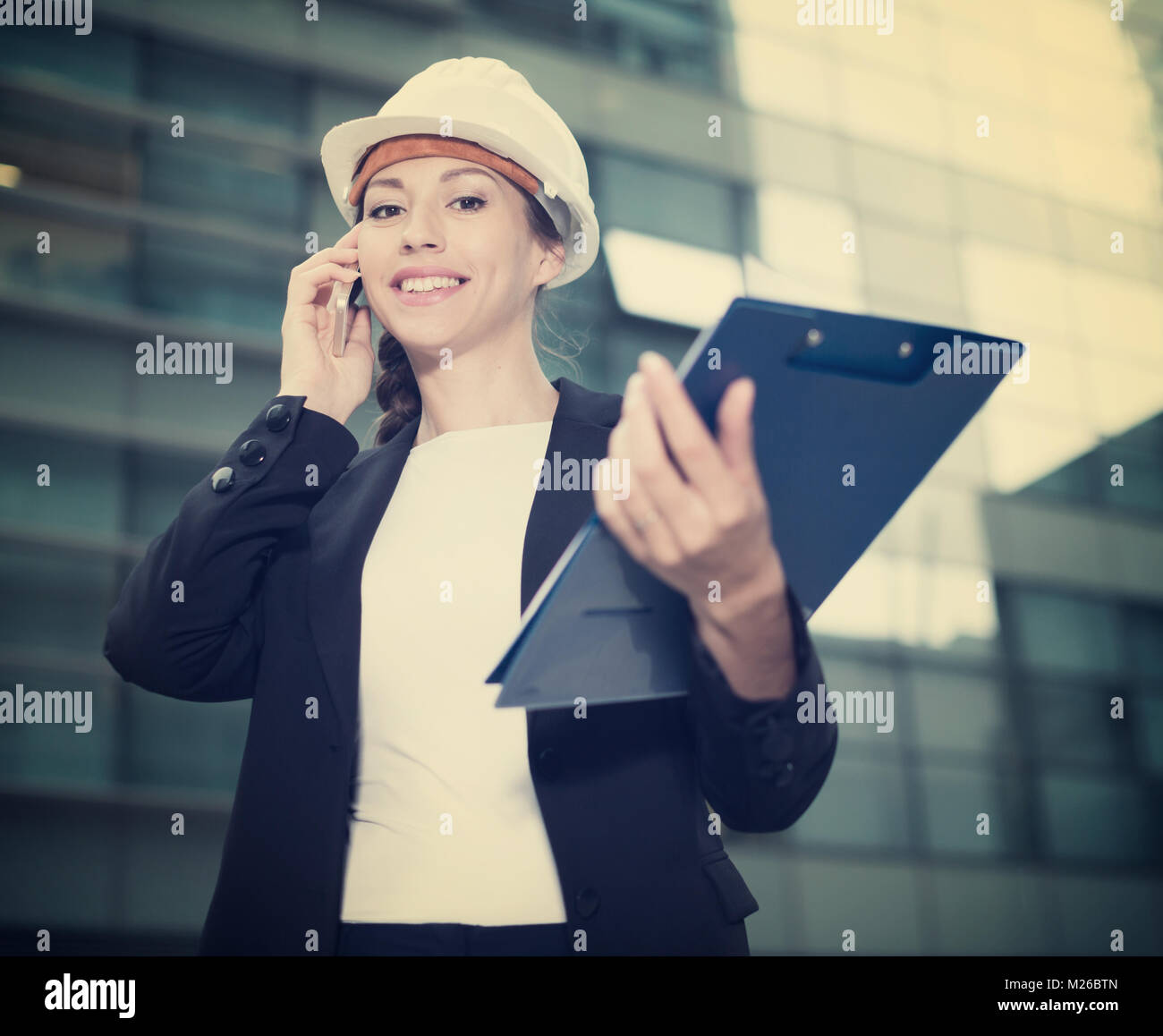 Woman architector in suit and hat is talking about project by the phone ...