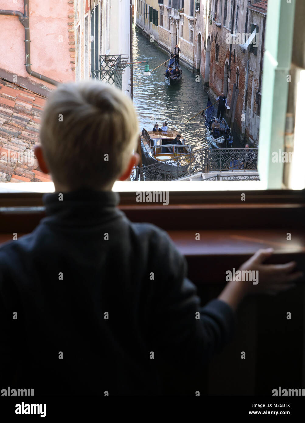 A young boy looks out a hotel window over a canal in Venice, Italy ...