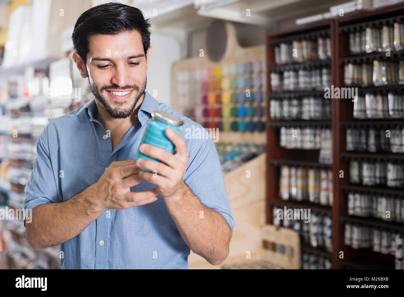 Smiling young man closely reading instruction on paint near racks in ...