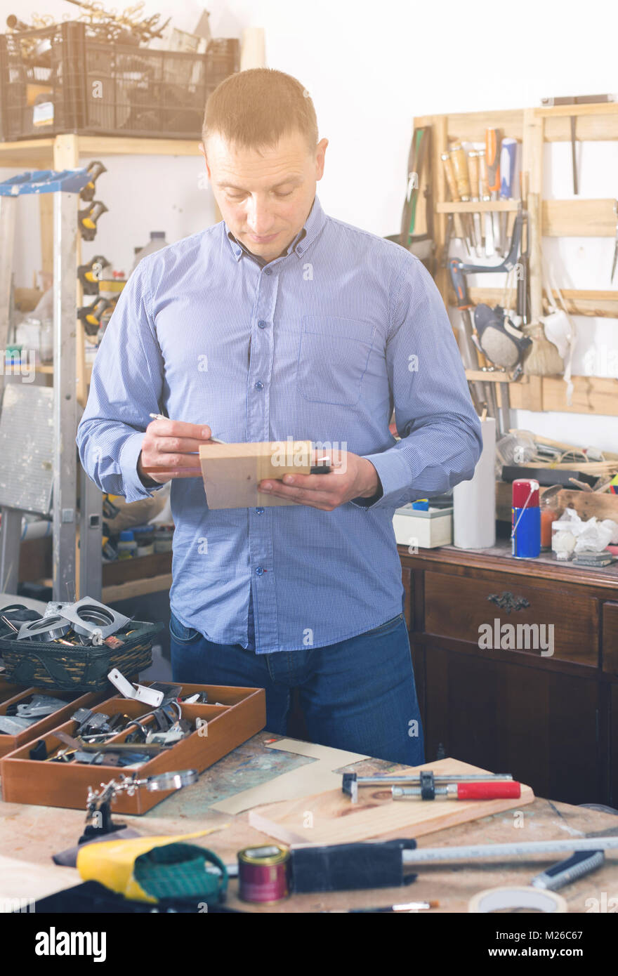 positive young spanish male carpenter working wood plank at workshop ...