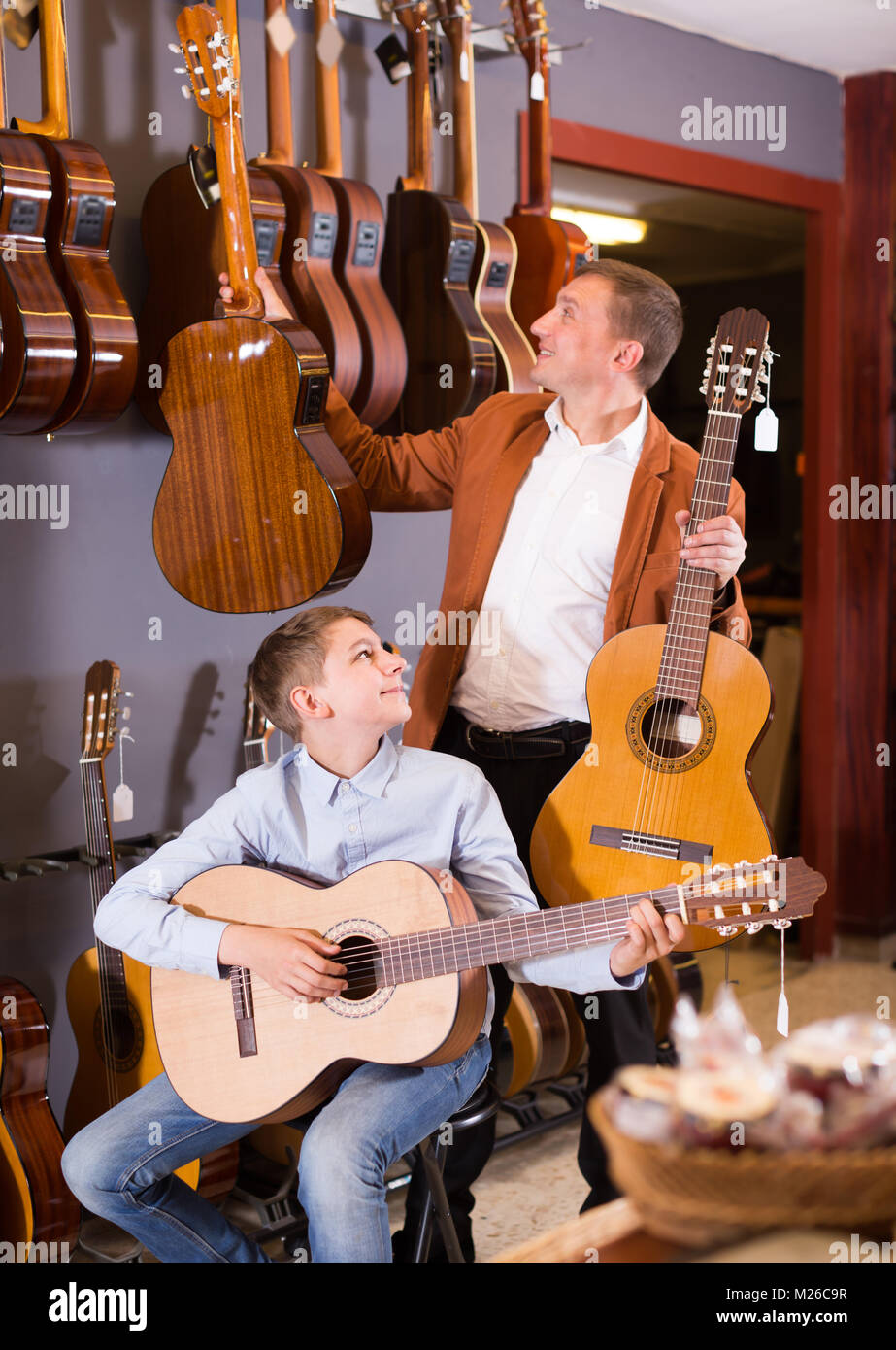 Ordinary seller showing acoustic guitar to boy client in musical shop ...