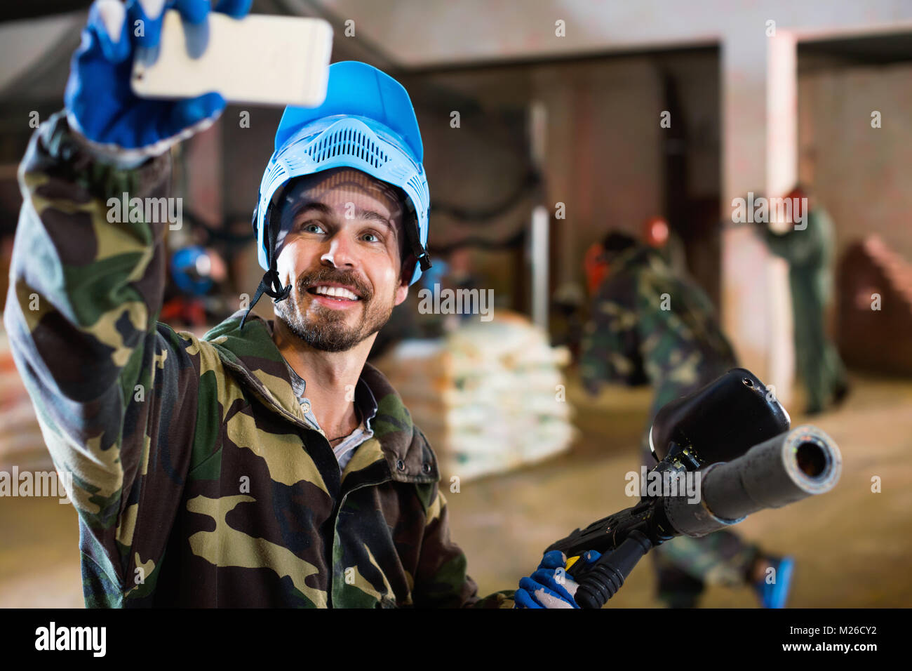 Young man in blue mask is making selfie on battlefield of paintball ...