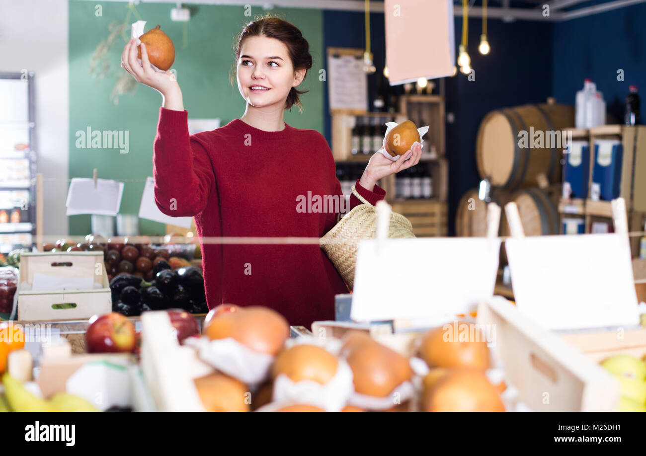 Portrait of smiling brunette girl buying ripe pear in supermarket Stock ...