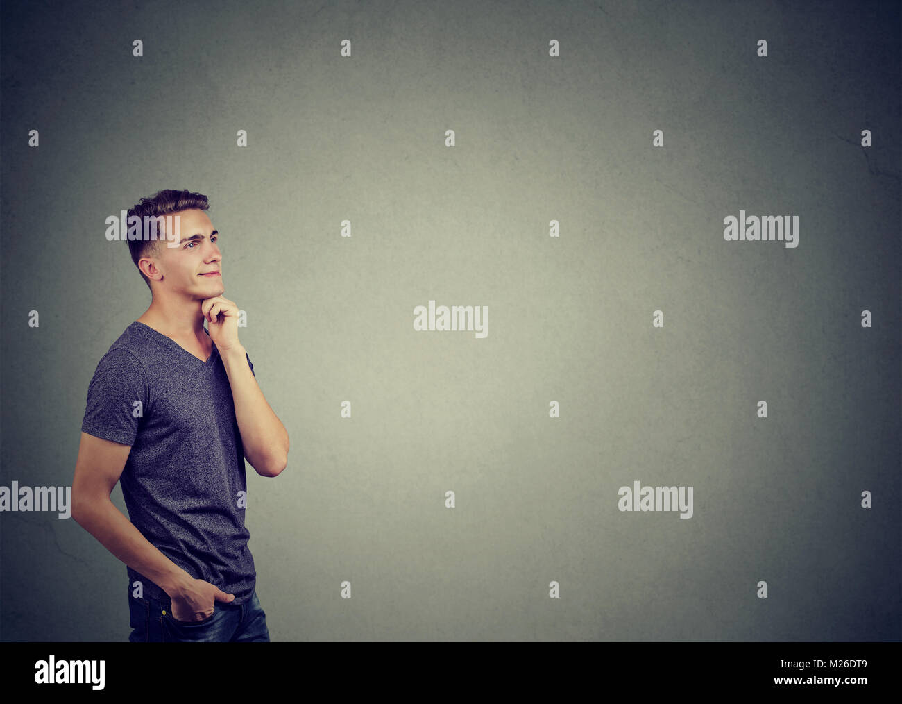 Thoughtful young casual man standing on gray backdrop and looking away ...