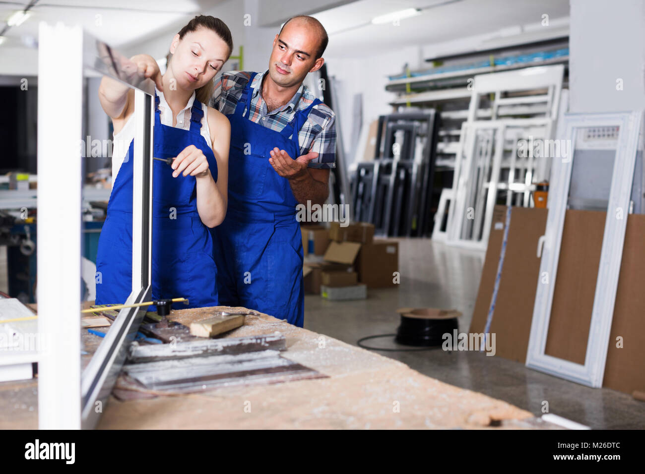 Team of two workers in blue overalls assembling pvc windows at factory ...