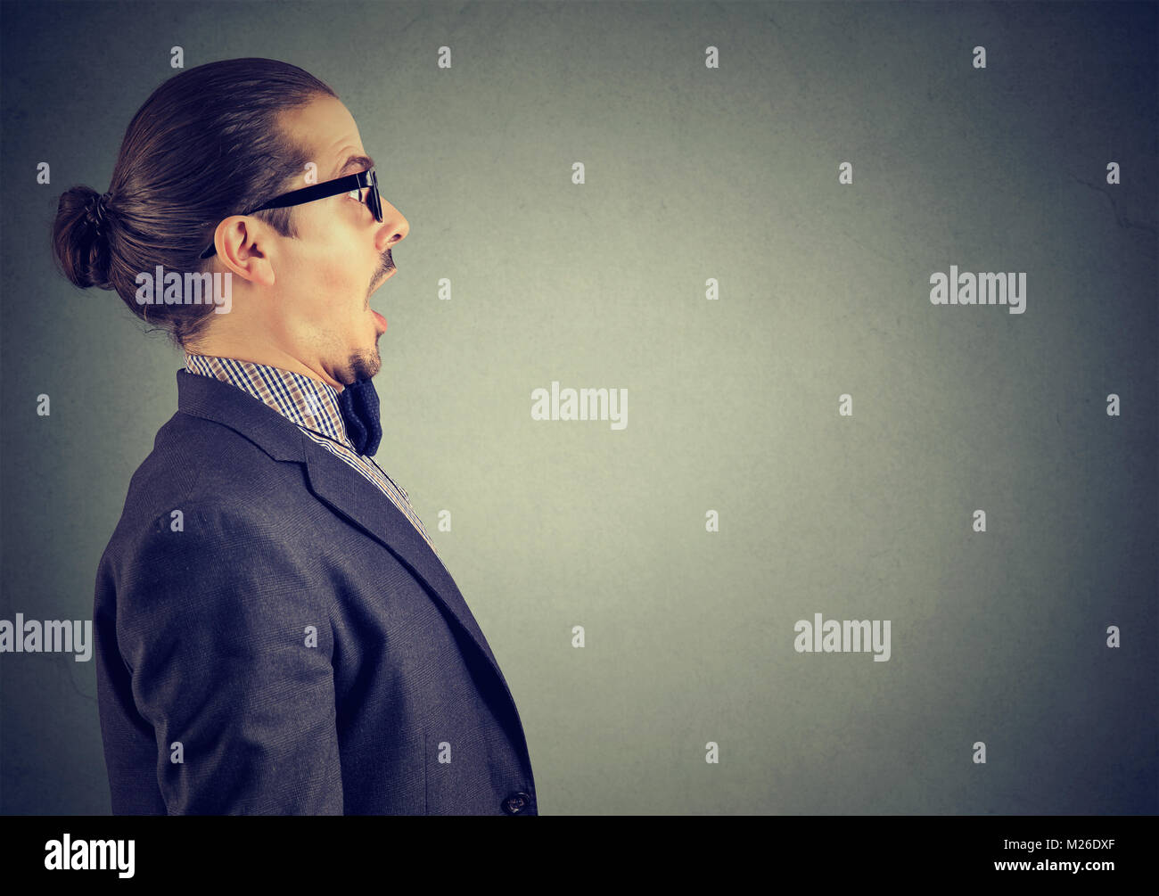 Side view of man in suit standing with mouth opened on gray looking ...