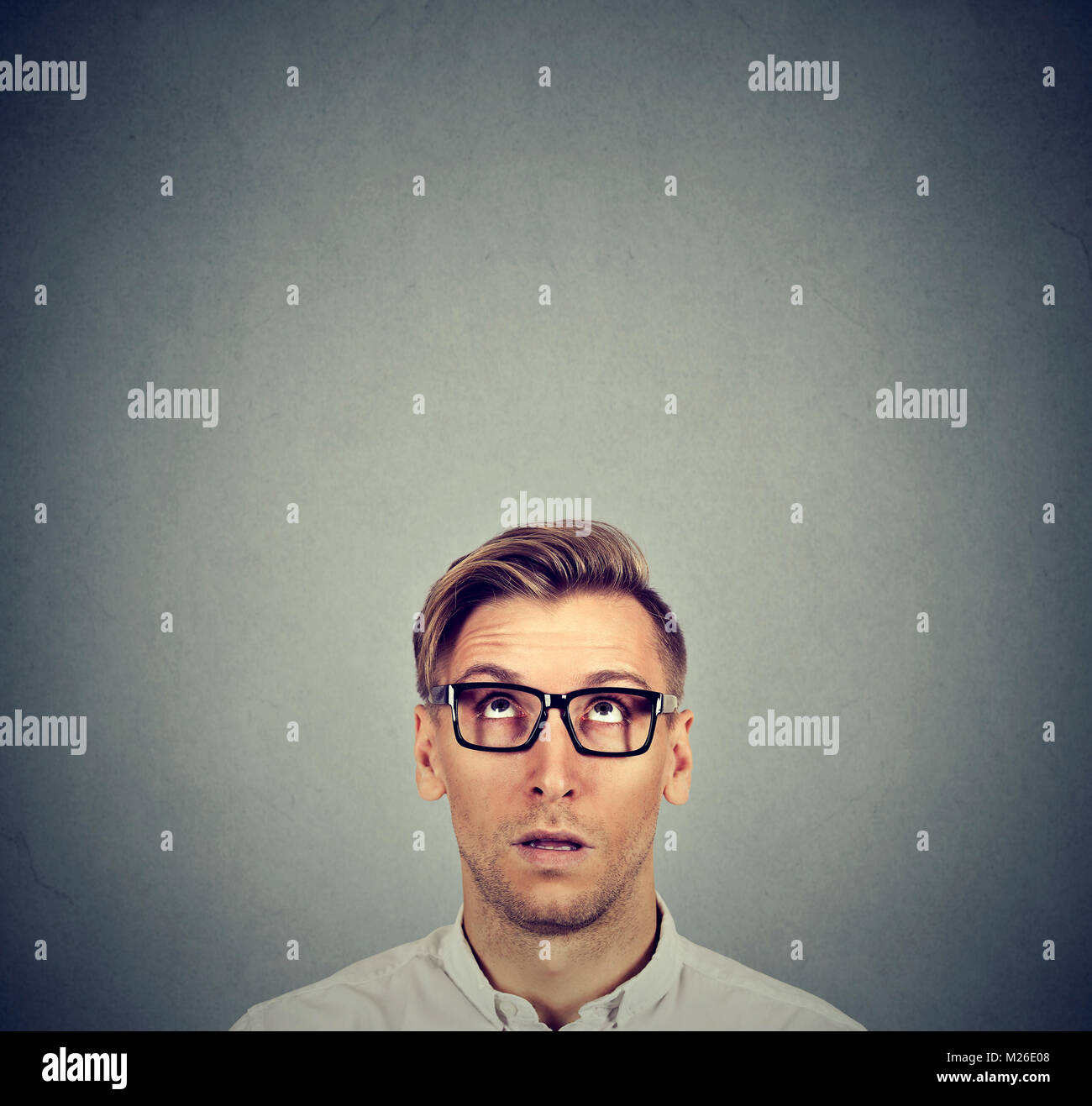 Young man in eyeglasses looking up posing on gray with expression of ...