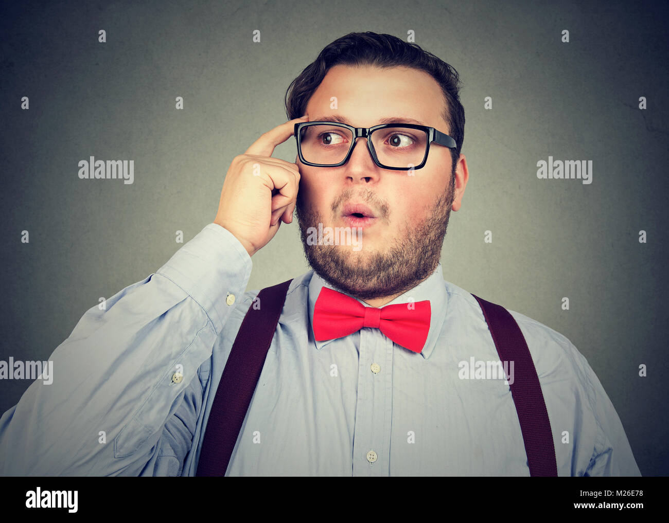 Young chubby man in eyeglasses touching temple looking puzzled while ...