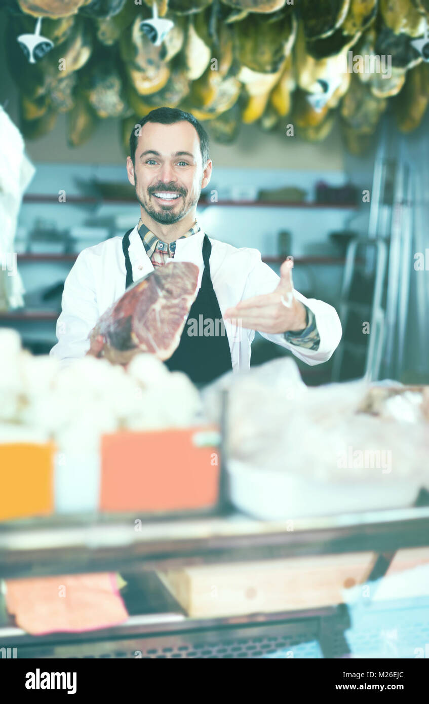 Smiling man assistant showing piece of meat in butcher’s store Stock ...