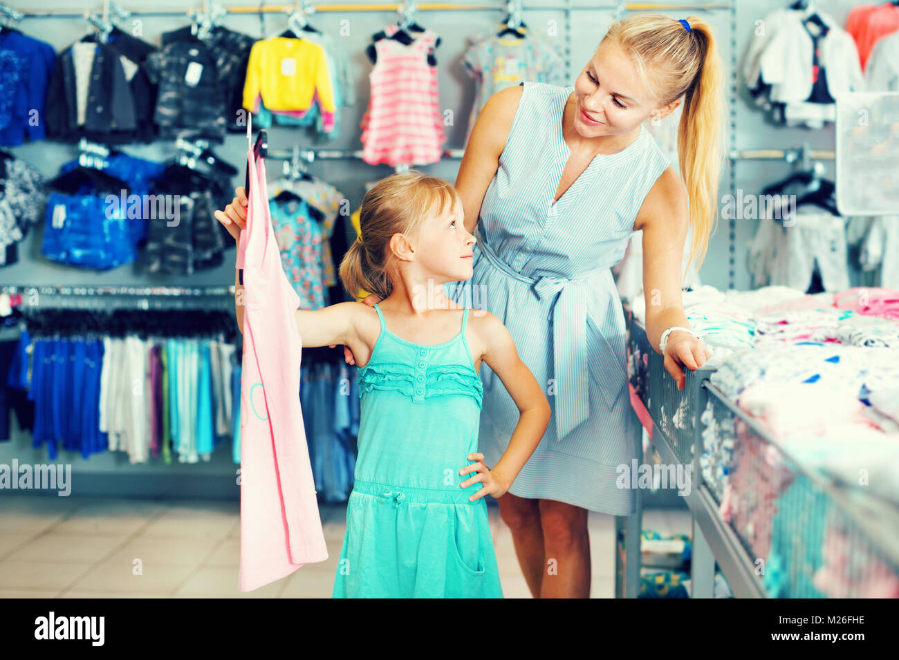 Happy cheerful positive female with girl choosing different clothes in ...