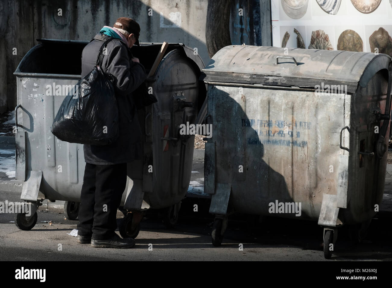 An elderly man searching in trash cans for utilizable things in the ...