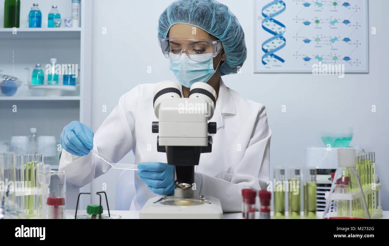 Biracial laboratory scientist doing medical research, looking at glass ...