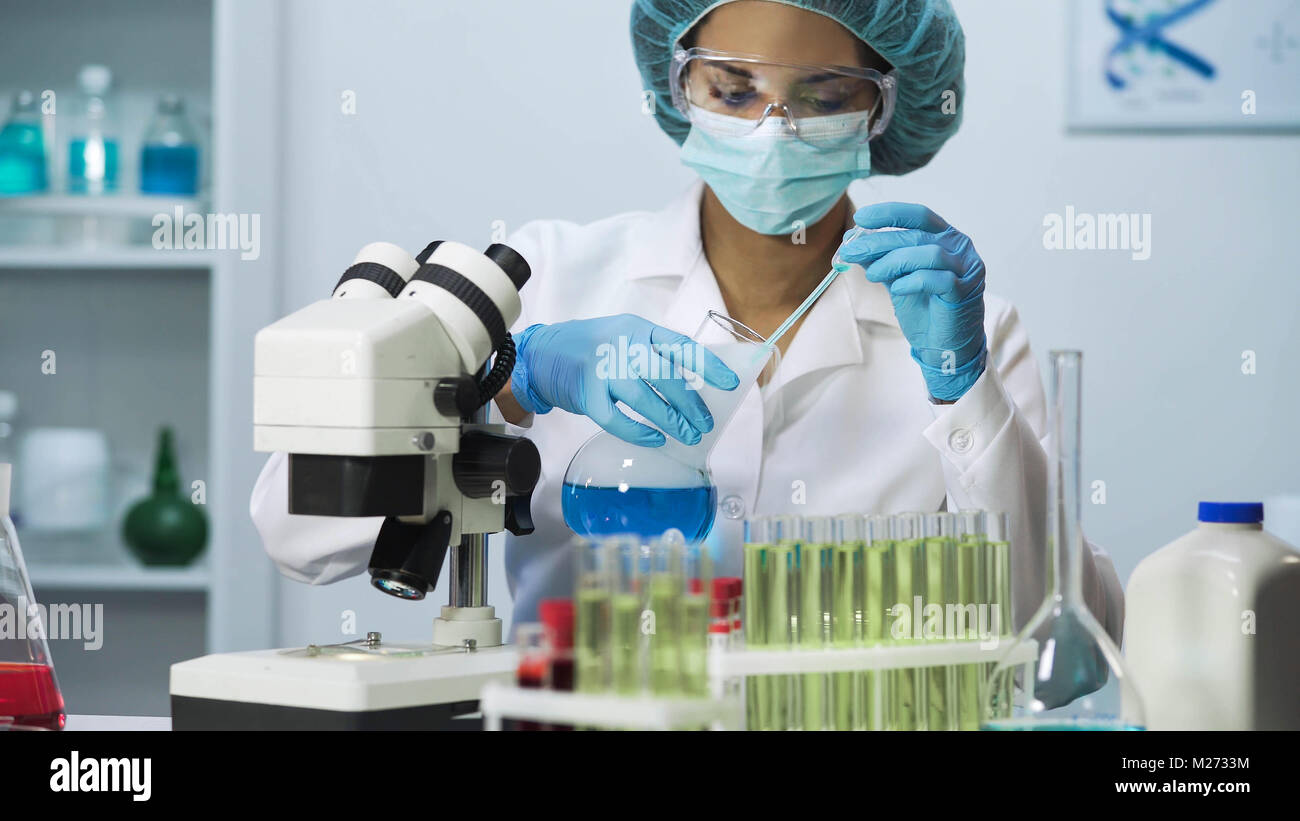 Young medic taking blue liquid sample and doing biochemical research ...
