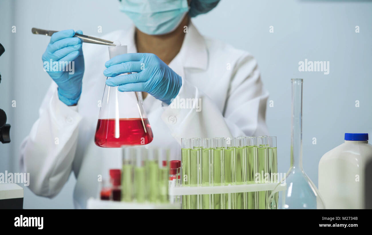 Female lab assistant putting reagent into the flask, doing cosmetology ...