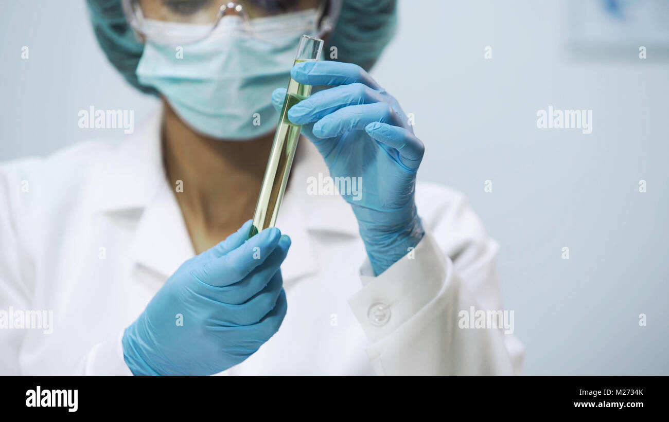 Lab worker holding tube with liquid, checking transparency, medical ...