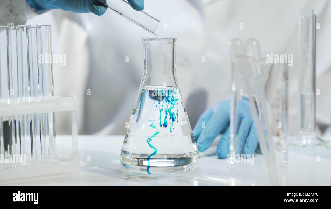 Chemist pouring substance into conical flask with liquid, chemical ...