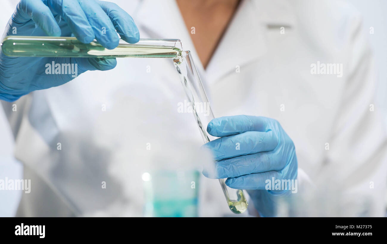 Medical worker pouring yellow liquid into test tube, perfume production ...