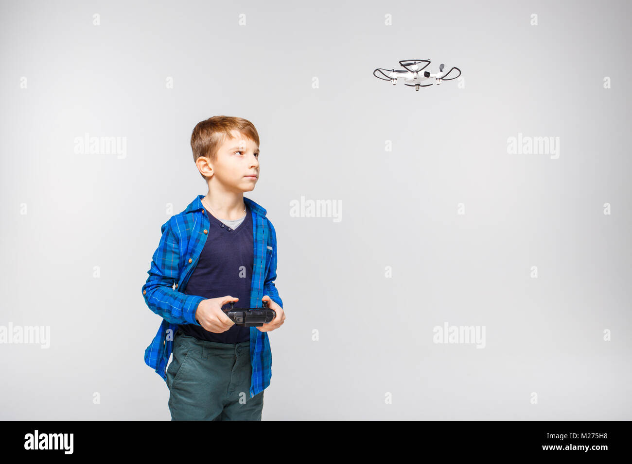 Cute boy operating the dron or quadcopter by remote control on grey ...