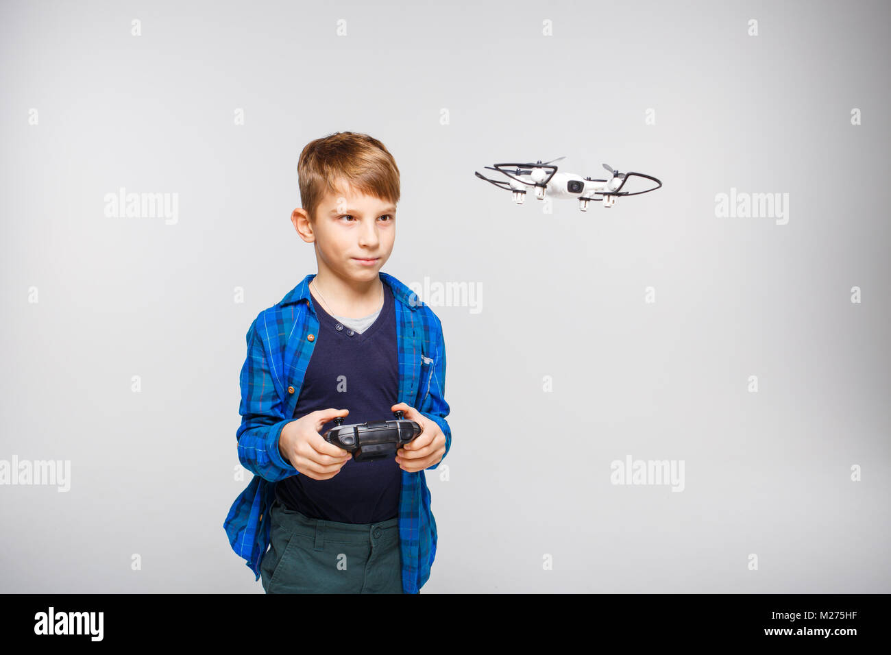 Cute boy operating the dron or quadcopter by remote control on grey ...
