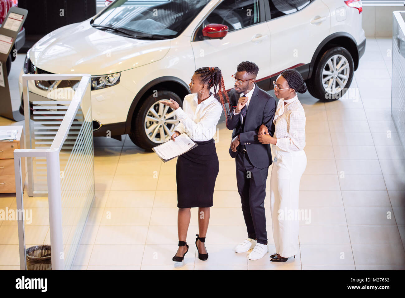 car salesman standing at dealership telling about features of car to ...