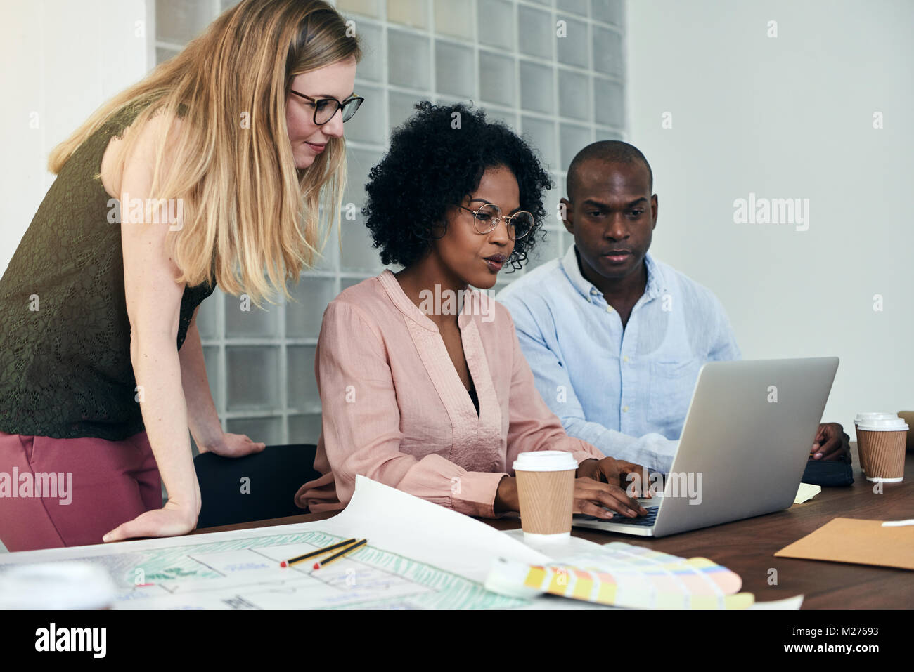 Diverse group of work colleagues working together on a laptop at a desk ...