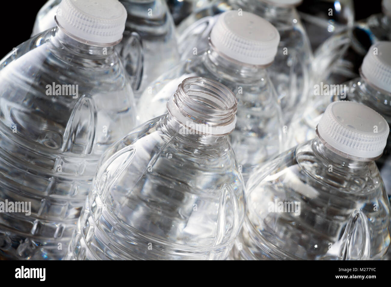 One open plastic bottle of water and other bottles closed on black ...