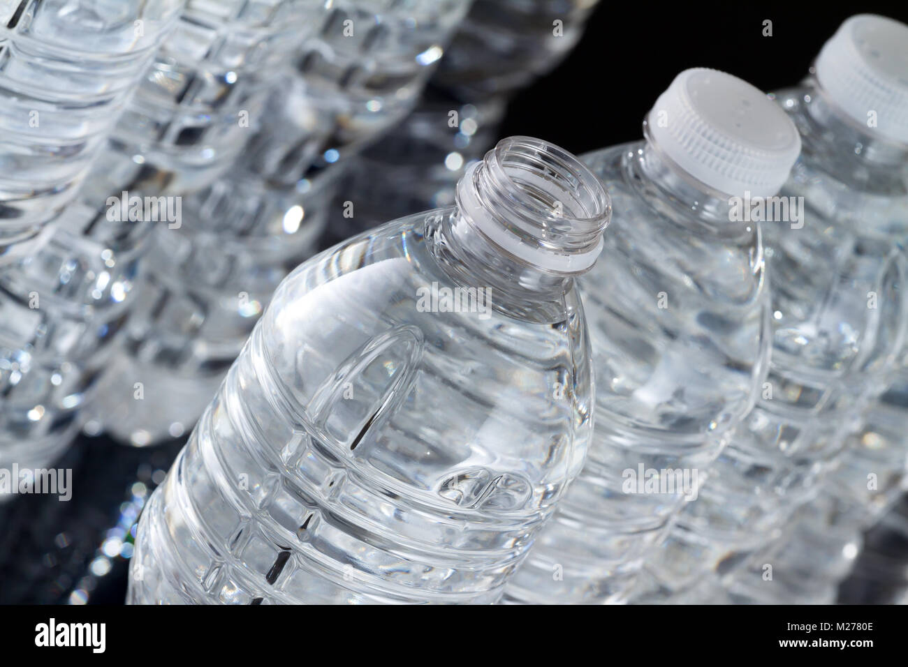 One open plastic bottle of water and other bottles closed on black ...