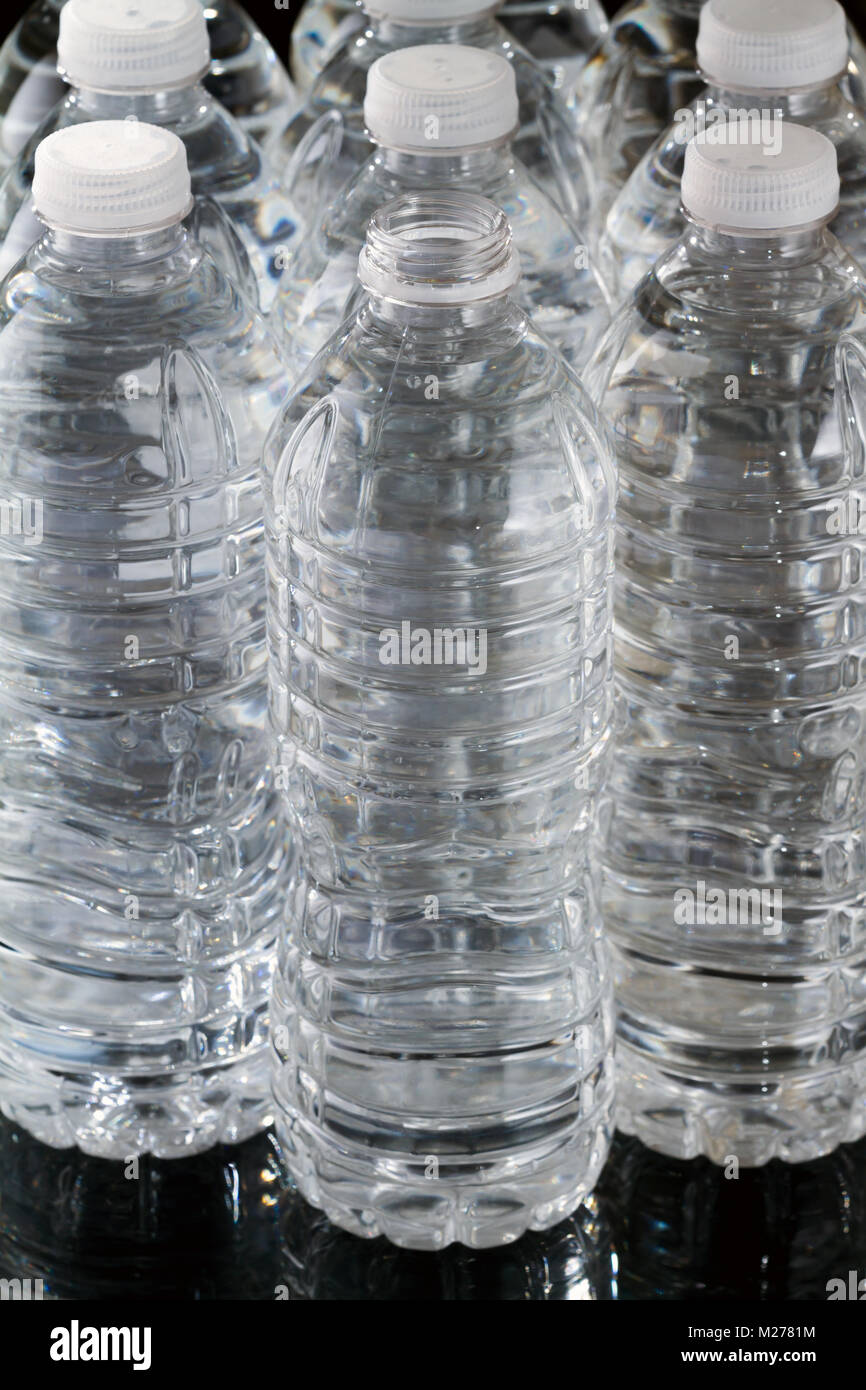 One open plastic bottle of water and other bottles closed on black ...