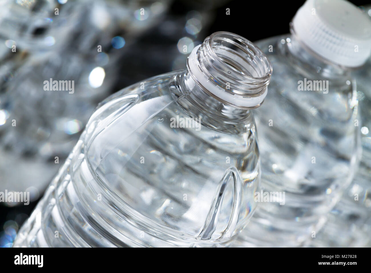 One open plastic bottle of water and other bottles closed on black ...