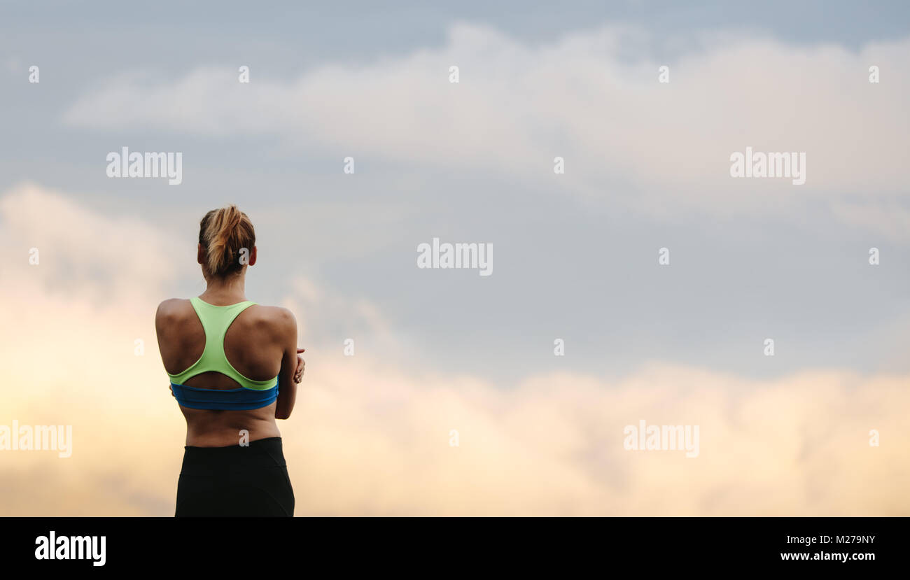 Rear view of woman athlete in running gear standing with hands folded ...