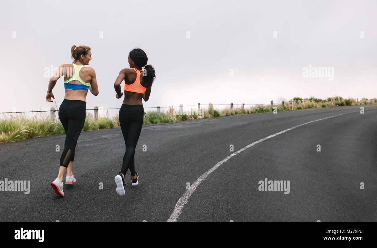 Rear view of two women athletes running on road early on a foggy ...