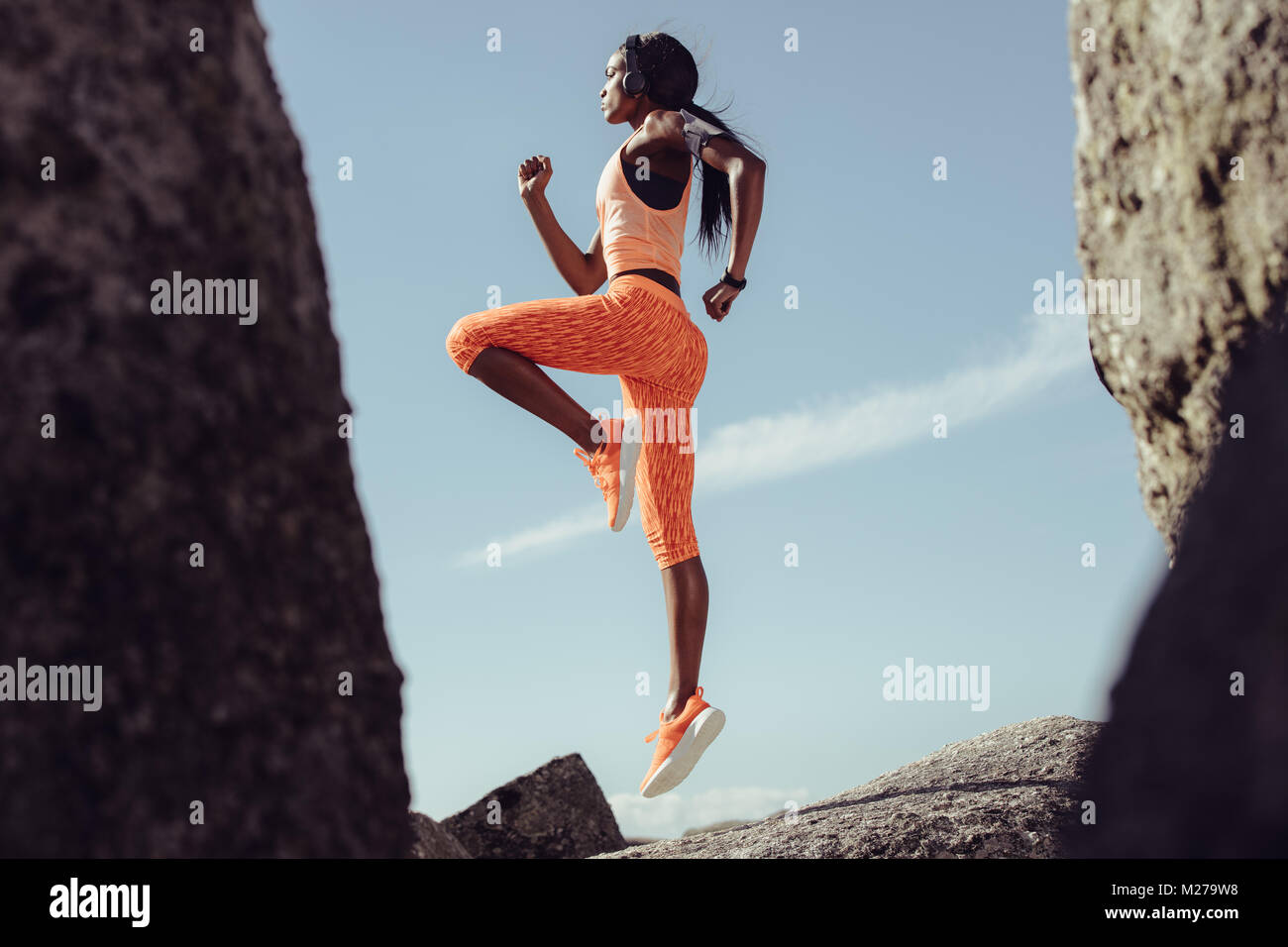 African female athlete jumping and stretching over rocks outdoors ...