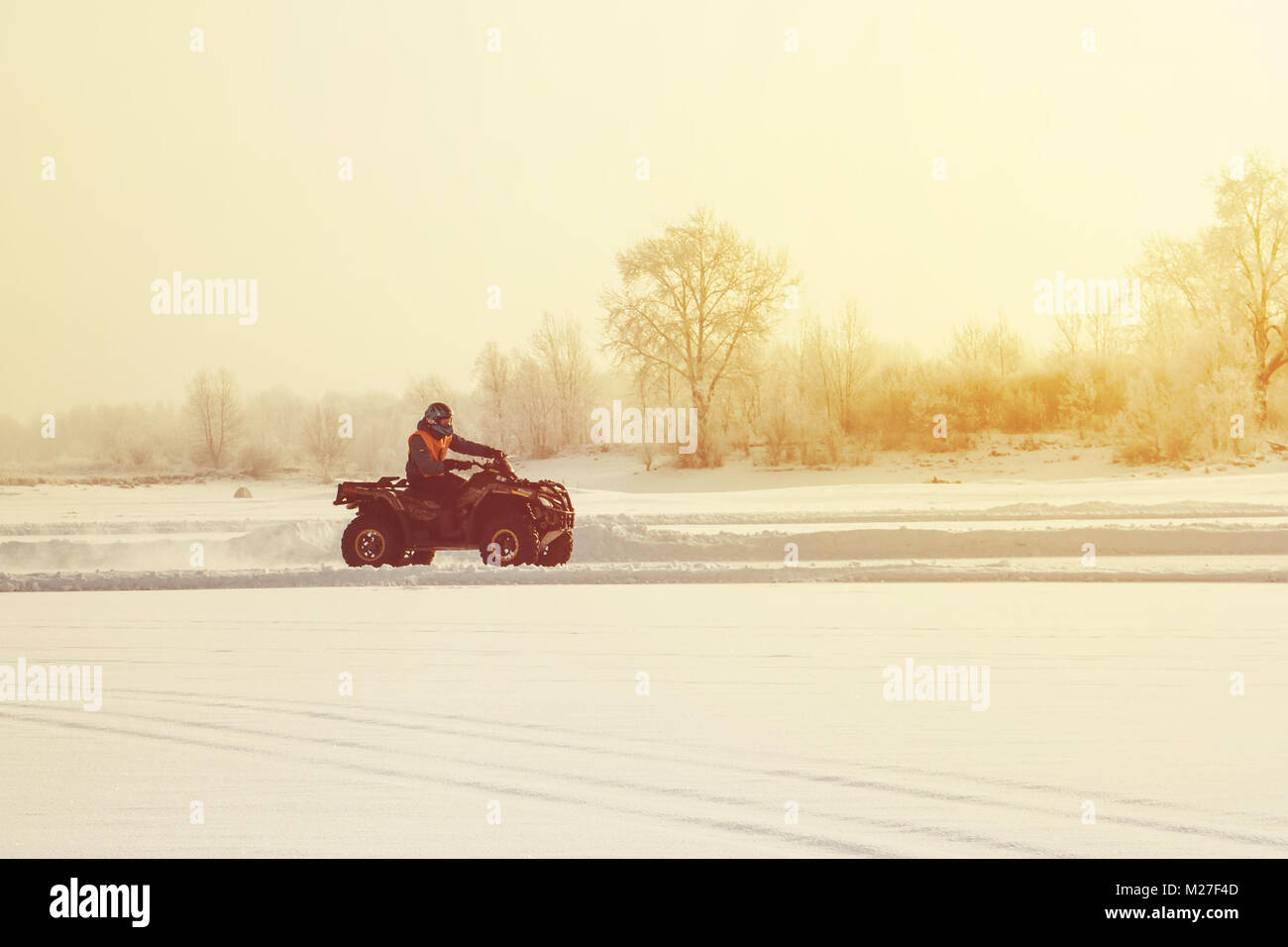 The ATV rider rides on the ice at sunset in winter, in winter the ...