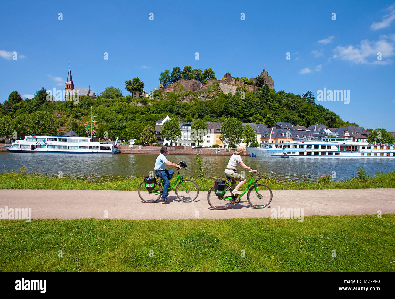 Cyclists on cycleway at riverside, excursion ship on the Saar river ...