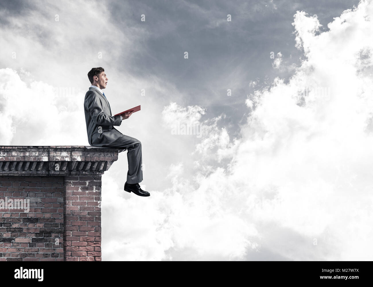 Man on roof edge reading book and cloudscape at background Stock Photo ...