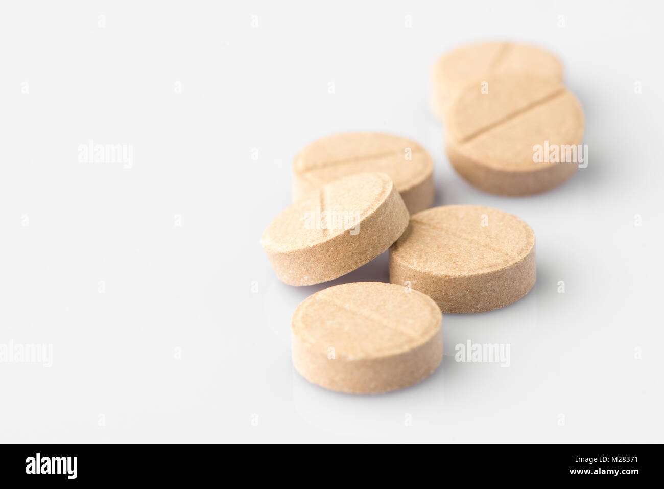 A pile of beige medical tablets on a light background. The blurred part ...