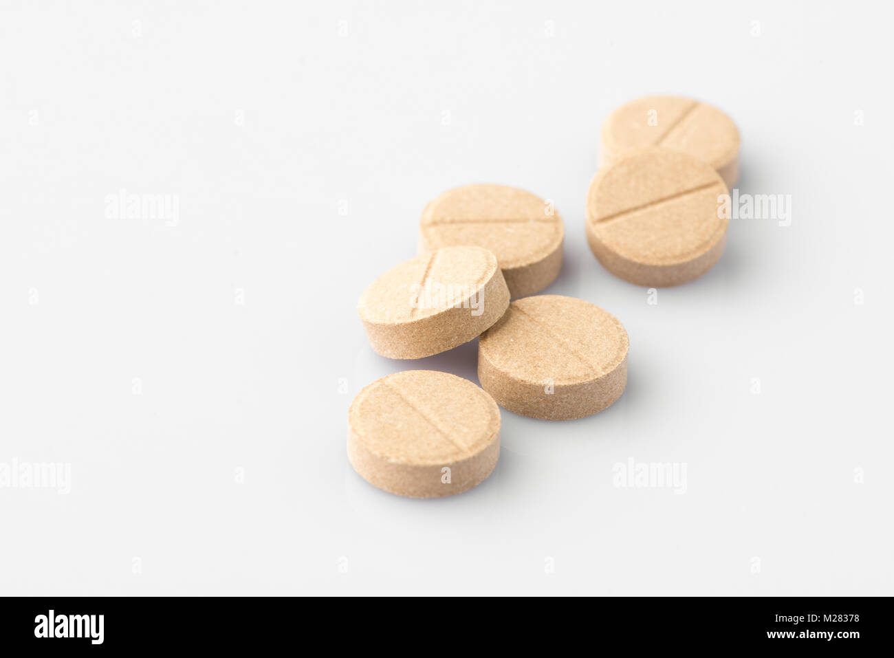 A pile of beige medical tablets on a light background. The blurred part ...
