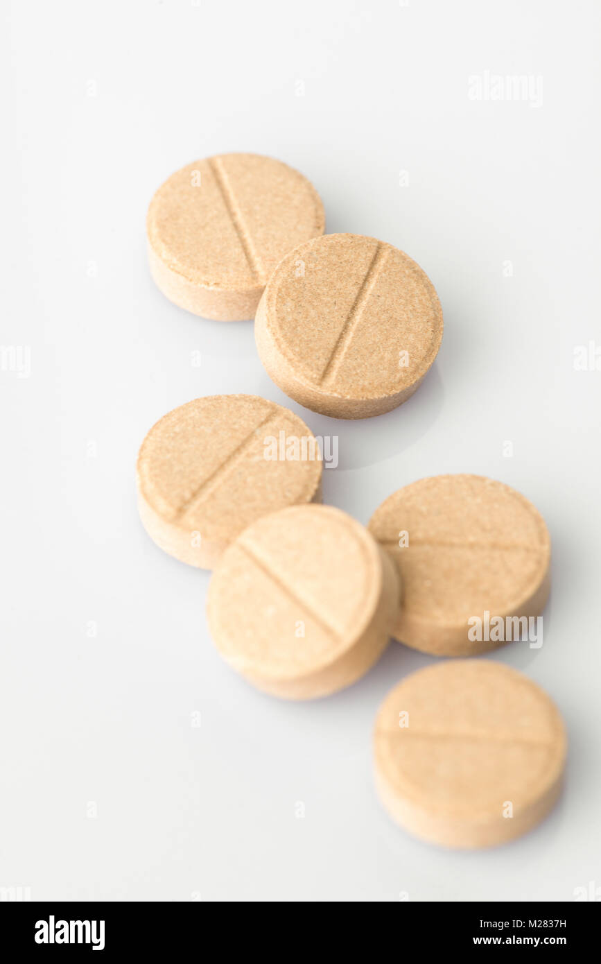 A pile of beige medical tablets on a light background. The blurred part ...