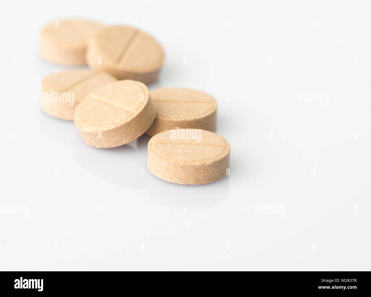 A pile of beige medical tablets on a light background. The blurred part ...
