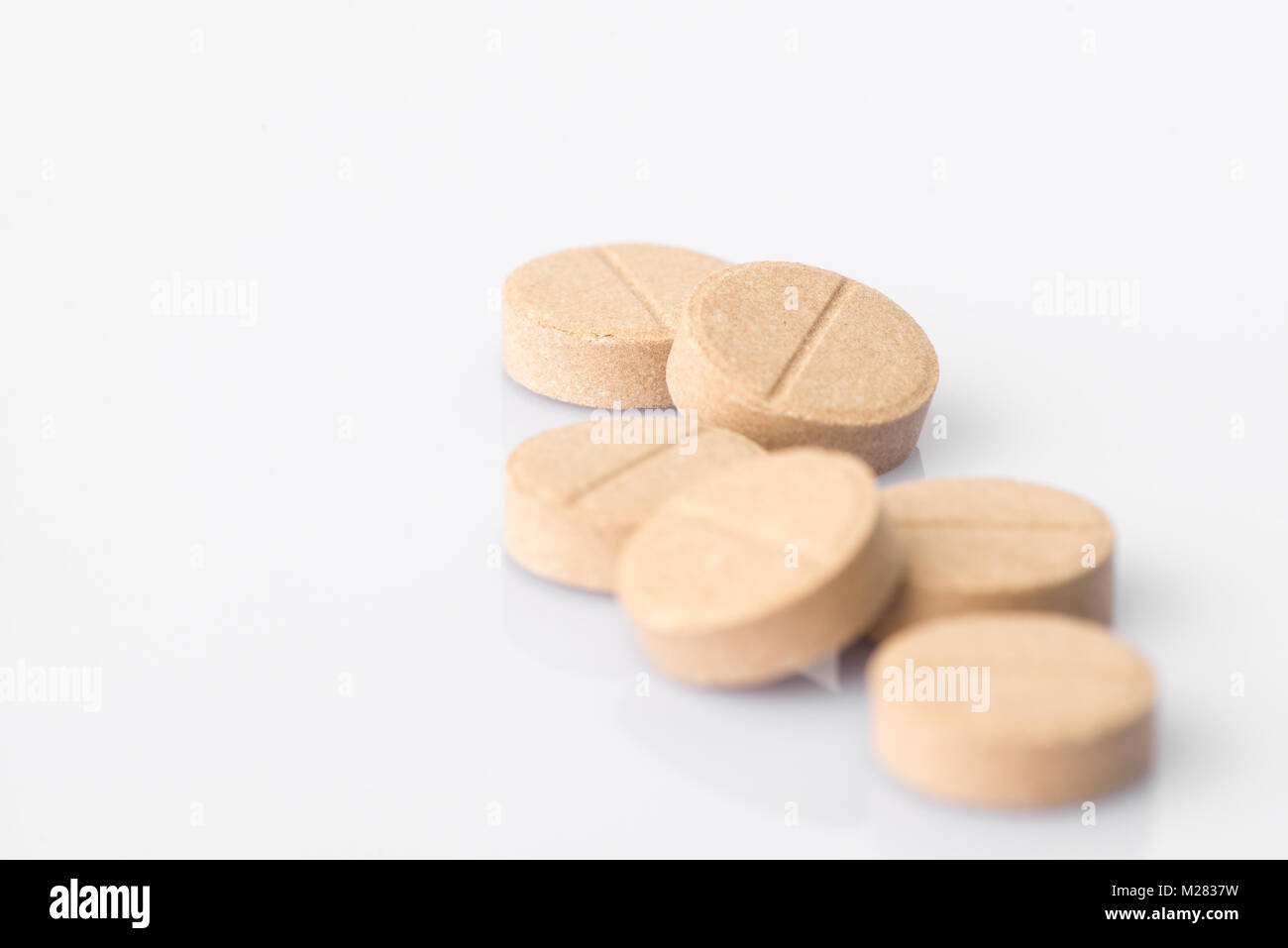 A pile of beige medical tablets on a light background. The blurred part ...